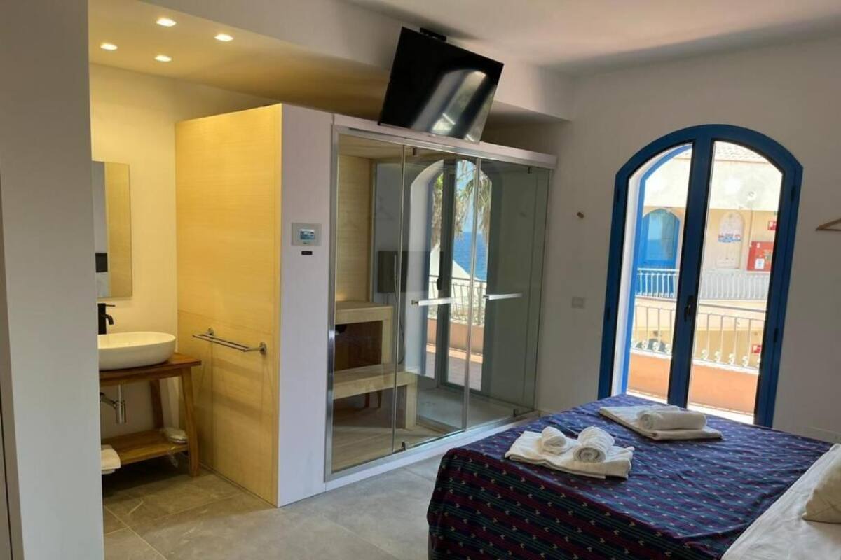 Quarto com cama, banheiro com pia e porta de vidro corrediça que dá para uma varanda.