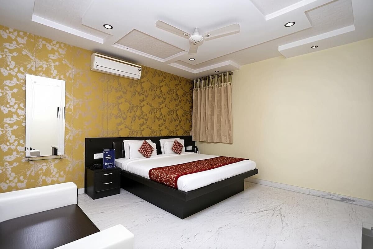 Quarto de hotel com cama, mesa de cabeceira, ar condicionado, ventoinha no teto e espelho.