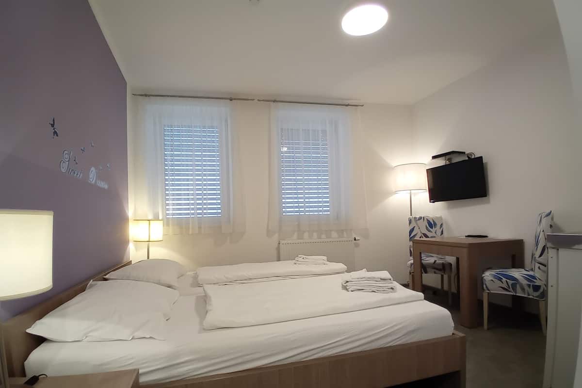 Quarto de hotel com cama, duas luminárias de cabeceira, uma televisão, uma escrivaninha e uma cadeira.