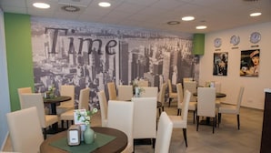Um restaurante com várias mesas e cadeiras, um mural com paisagem urbana na parede, e relógios na parede.