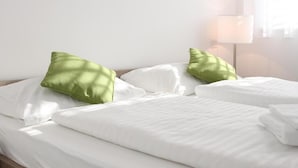 Uma cama com roupa de cama branca e almofadas verdes, um abajur e uma janela com cortinas.