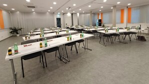 Sala de conferências com várias mesas, cadeiras e garrafas de água.