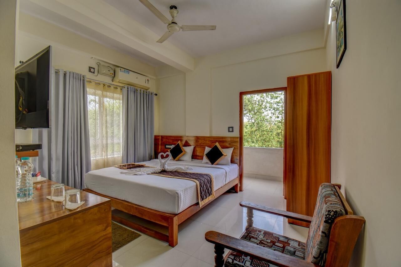 Quarto de hotel com cama, escrivaninha, cadeira, televisão e janela.