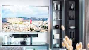 Uma sala de estar moderna com televisão de tela plana, sofás cinzas, uma estante preta e iluminação pendente.