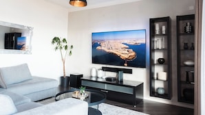 Uma sala de estar moderna com uma televisão de tela plana grande, um sofá, uma mesa de centro e uma planta decorativa.