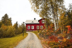 Uma casa vermelha com um caminho de cascalho que a leva, rodeada por folhagem de outono.