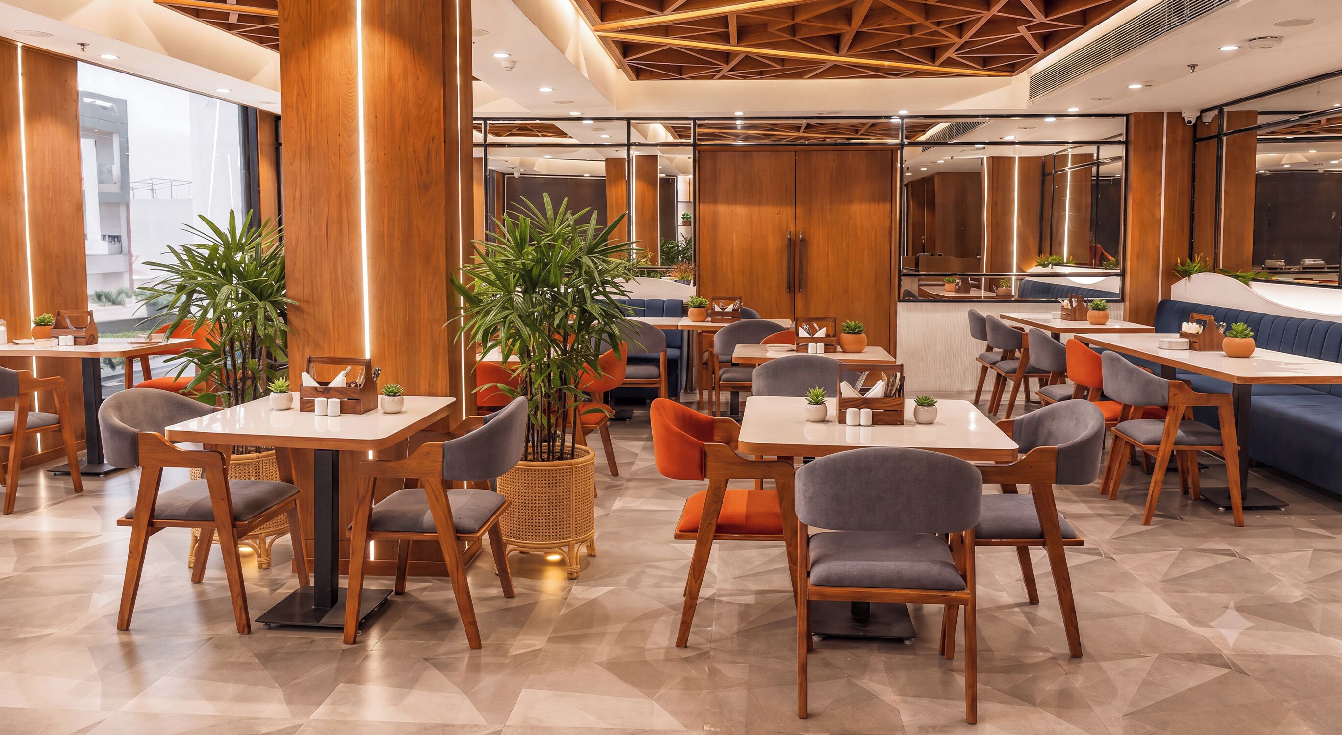 Interior de restaurante moderno com mesas e cadeiras de madeira, plantas em vasos e design geométrico no teto.