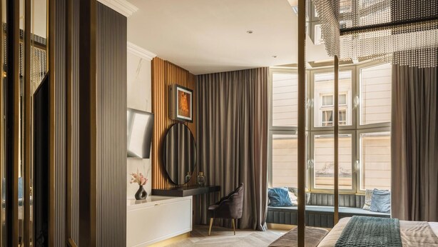 Quarto de hotel moderno com uma janela grande, uma cama, área de estar e televisão fixada na parede.