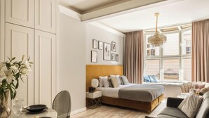 Quarto com cama, mesa de cabeceira, luminária e janela com cortinas.