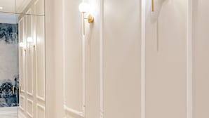 Um corredor com paredes brancas e detalhes dourados, incluindo arandelas e uma porta com puxador dourado.