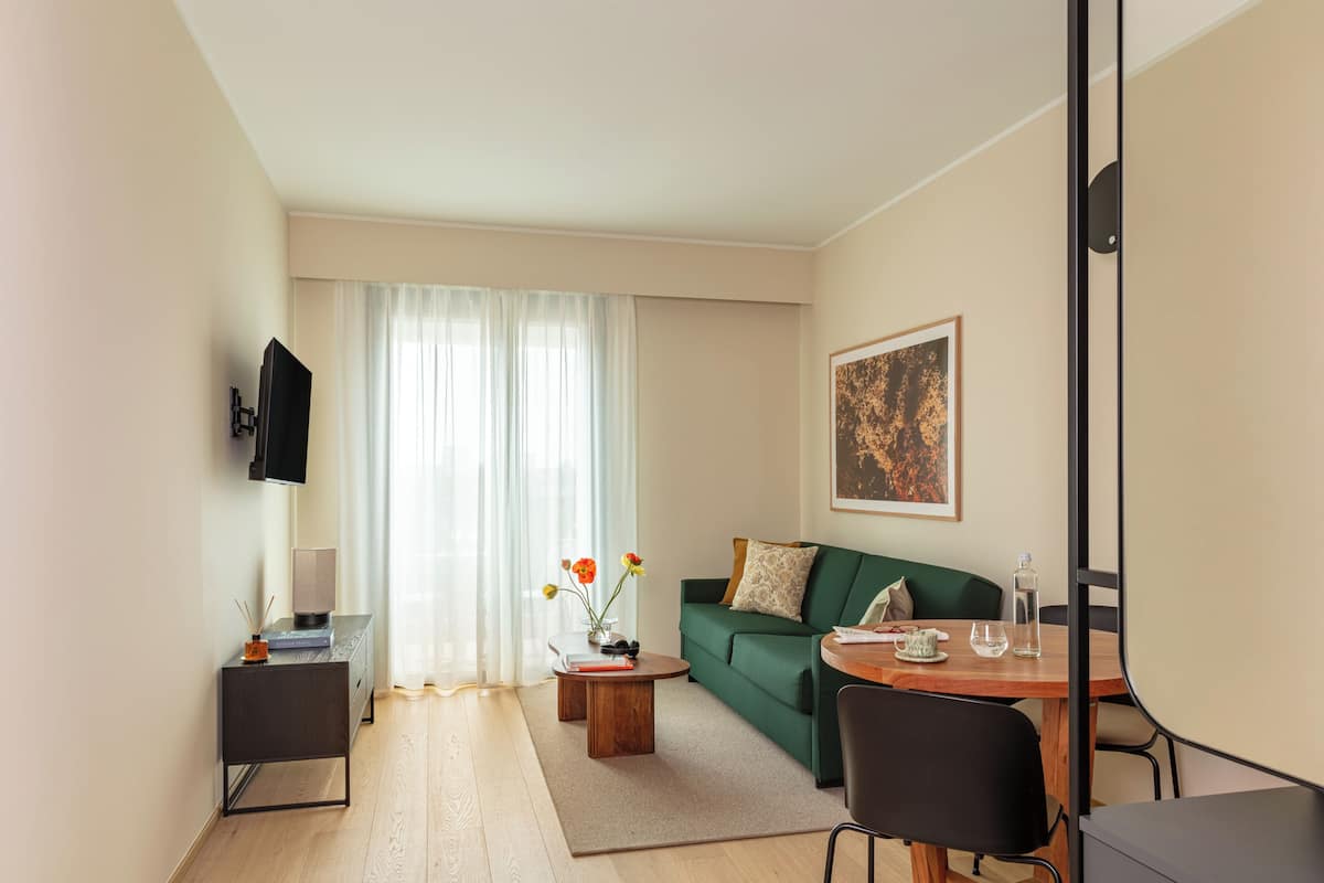 Uma sala de estar moderna com uma televisão de tela plana, um sofá verde, uma mesa de centro de madeira e uma mesa de jantar com cadeiras.