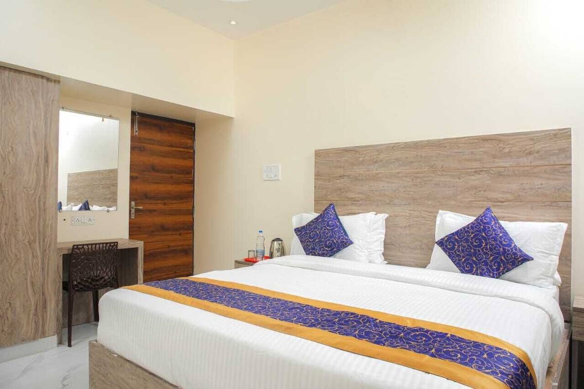 Quarto de hotel com cama, escrivaninha, cadeira, cabeceira de madeira e espelho.