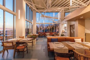 Um restaurante moderno com pé direito alto, grandes janelas e uma variedade de assentos, incluindo mesas e cabines.