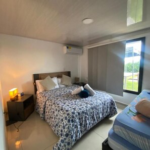Quarto com cama, mesa de cabeceira, abajur e janela com vista.