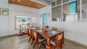 Uma sala de jantar com mesa de madeira posta para quatro, janela com vista e parede de tijolos brancos.