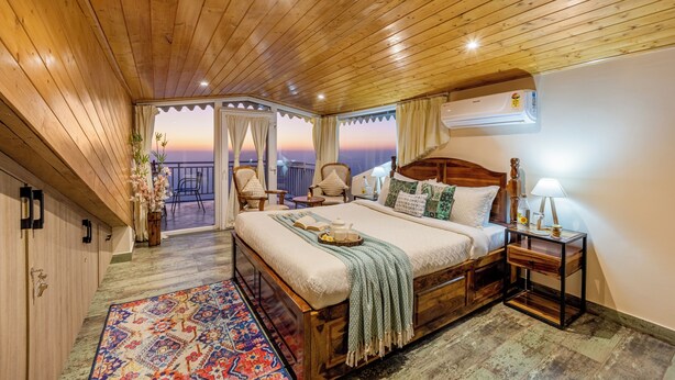 Quarto com painéis de madeira, uma cama, mesa de cabeceira e vista para o pôr do sol.