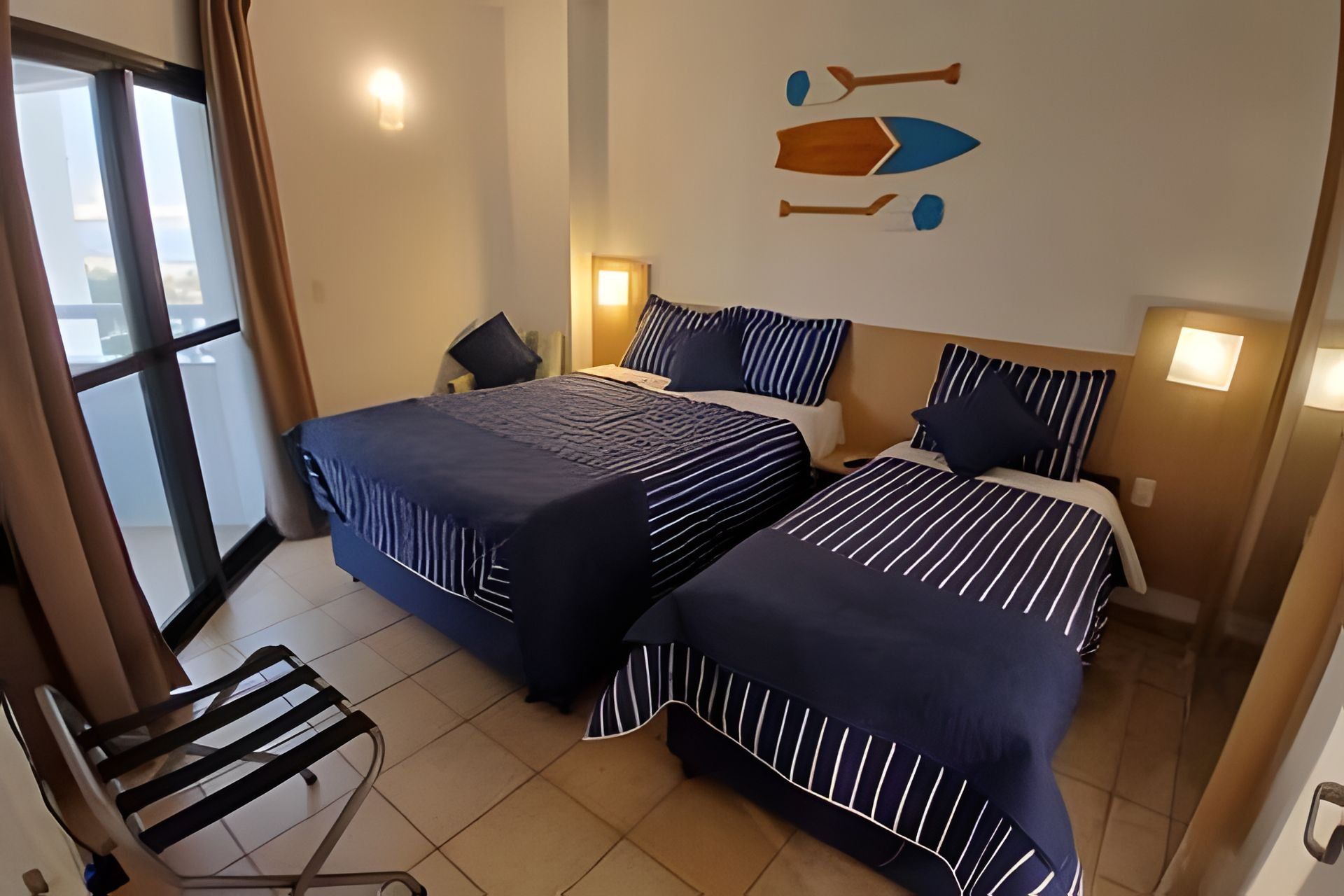 Quarto de hotel com duas camas, uma cadeira e vista para o exterior.
