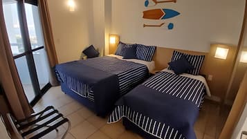 Quarto de hotel com duas camas, uma cadeira e vista para o exterior.
