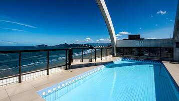 Piscina moderna no terraço, com vista para o oceano e montanhas ao longe.