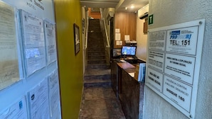 Corredor de hotel com balcão de recepção, escada e vários avisos informativos.