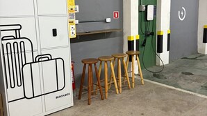 Um armário de serviço amplo, branco, com a etiqueta 'BEACH.BOX', painéis elétricos, uma porta verde e uma fileira de bancos de madeira.