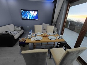 Uma sala de jantar com uma mesa posta para dois, uma televisão na parede e uma varanda com vista.
