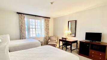 Quarto de hotel com duas camas, uma escrivaninha com cadeira, televisão e janela com cortinas.