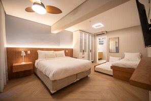 Quarto de hotel moderno com uma cama grande, uma cama menor, uma escrivaninha, uma cadeira, uma televisão e um guarda-roupa.