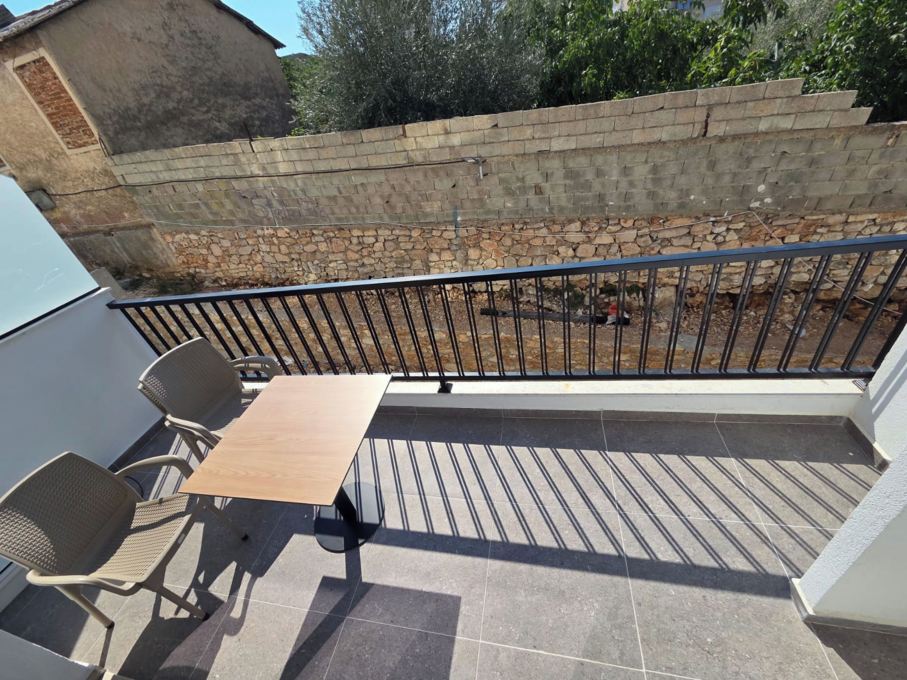 Varanda com mesa e cadeiras, parede de pedra e grade de metal.