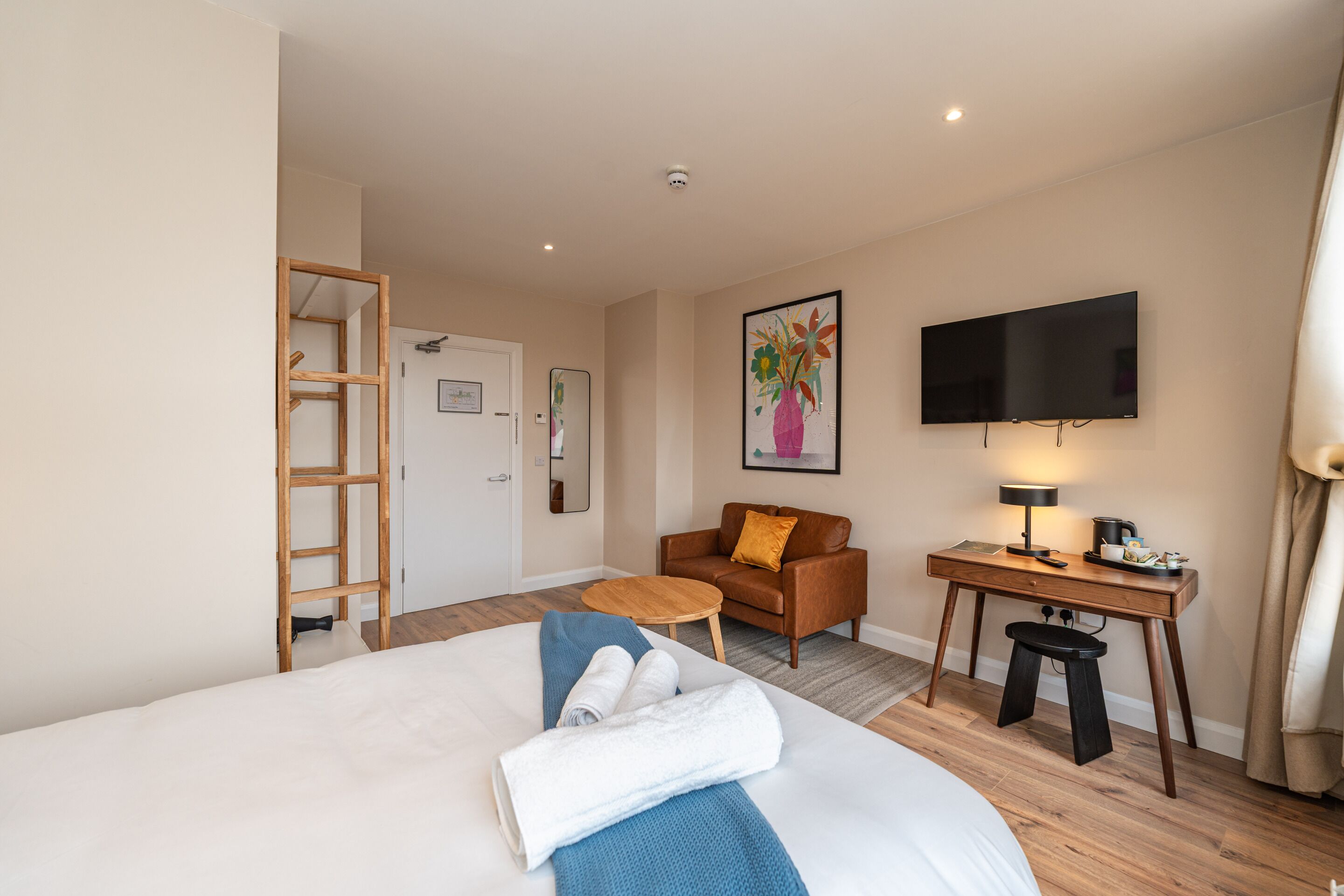 Quarto de hotel com uma cama, escrivaninha, cadeira, televisão e um quadro na parede.