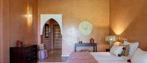 Quarto com cama, mesa de cabeceira, abajur, cômoda, tapete e uma porta em arco.
