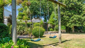 Um jardim com baloiço, um muro de pedra e um edifício ao fundo.