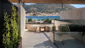 Uma área de estar moderna ao ar livre, com vista para uma vila costeira e montanhas.