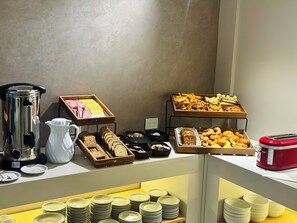 Um buffet de café da manhã com diversos alimentos, uma cafeteira e pilhas de pratos.