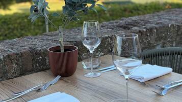Mesa posta ao ar livre com um vaso de planta, copos de vinho e talheres.