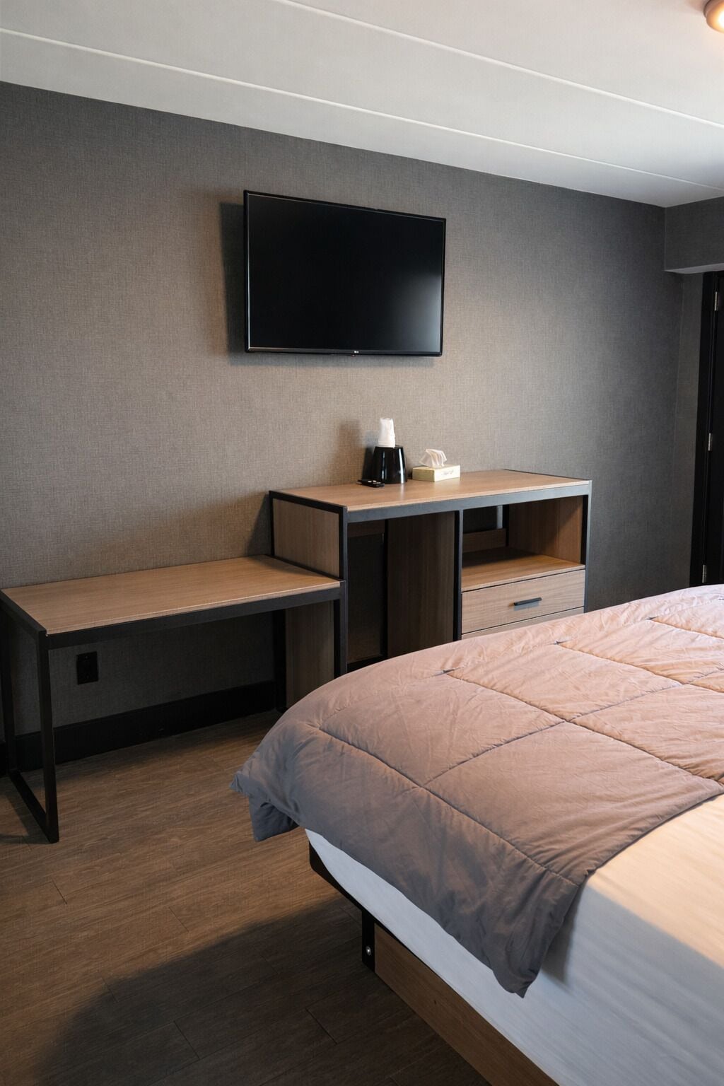 Quarto com cama, escrivaninha, televisão de tela plana e mesa de cabeceira com caixa de lenços e uma xícara.