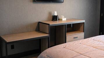 Quarto com cama, escrivaninha, televisão de tela plana e mesa de cabeceira com caixa de lenços e uma xícara.