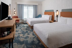 Quarto de hotel com duas camas, uma escrivaninha, televisão de tela plana, cafeteira e minibar.