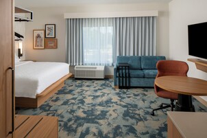 Quarto de hotel com cama, sofá, televisão e uma pequena mesa.