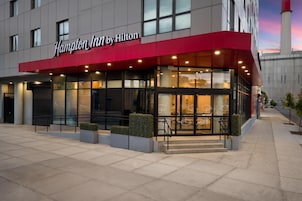 Um hotel Hampton Inn by Hilton com fachada moderna, grandes janelas e toldo vermelho.