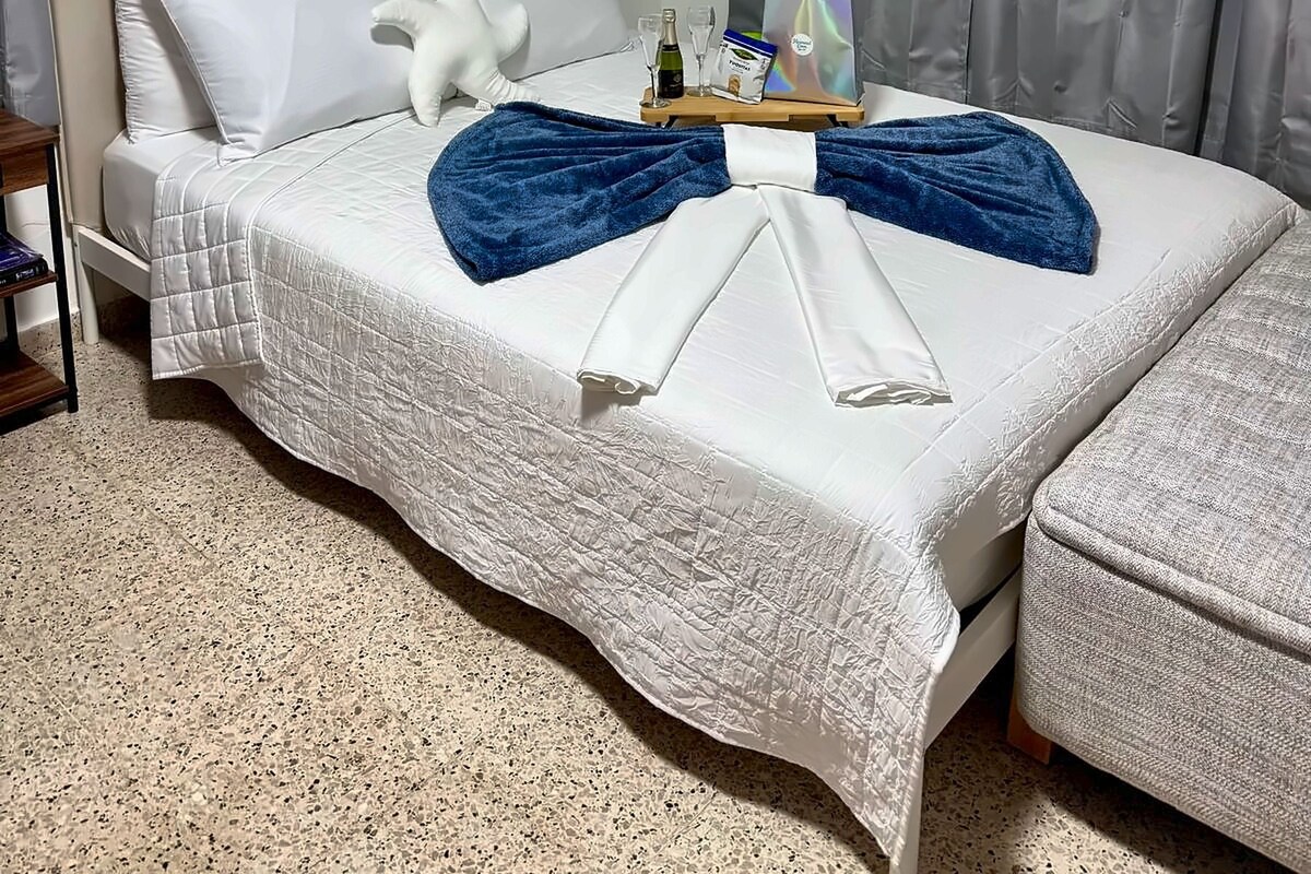 Quarto de hotel com cama, mesa de cabeceira, um quadro e janela com cortinas.