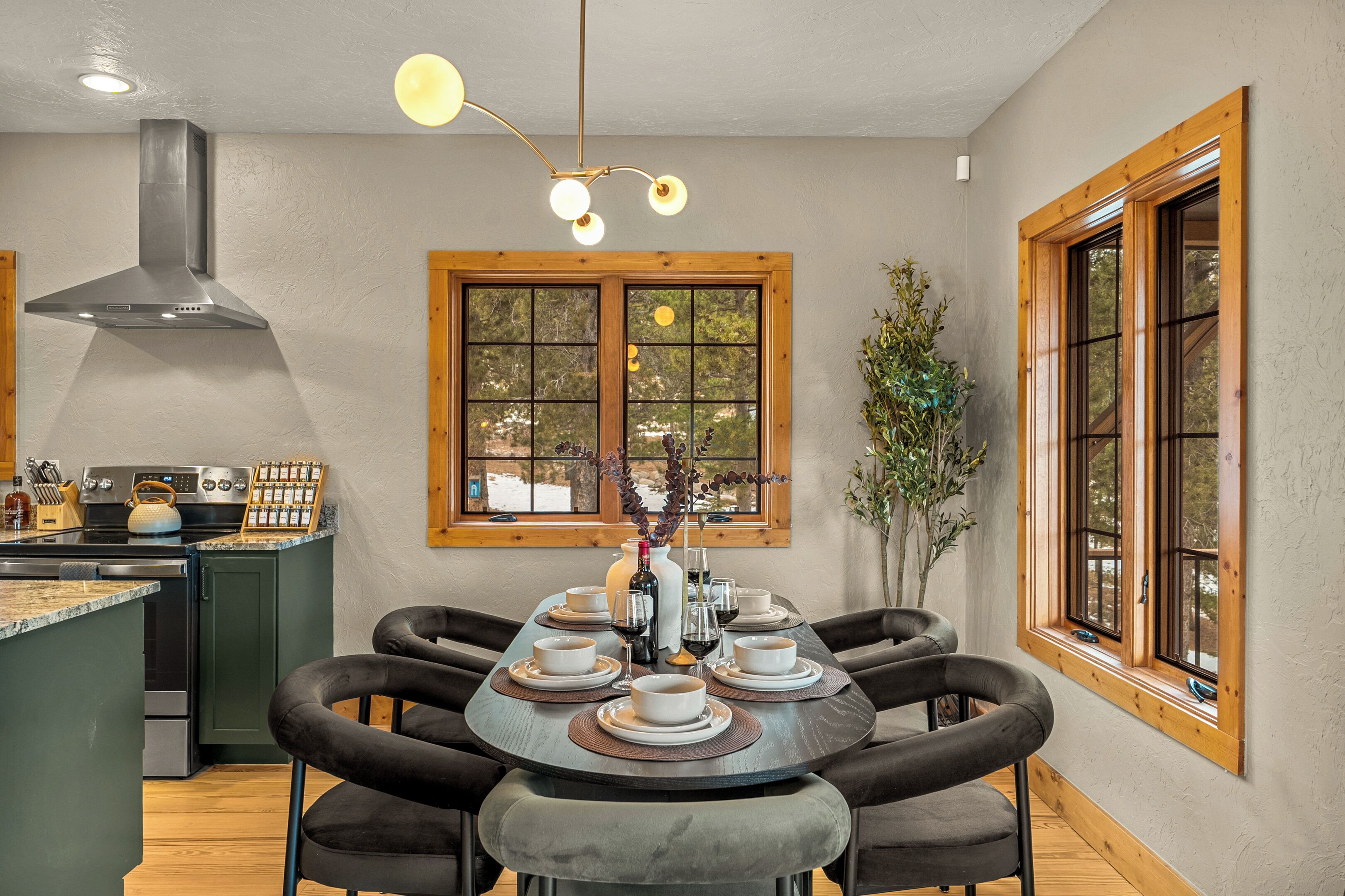 Uma sala de jantar com mesa redonda posta para seis, cozinha ao fundo e uma janela grande com vista.