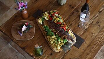 Uma mesa de madeira com peixe, legumes e uma garrafa de vinho.