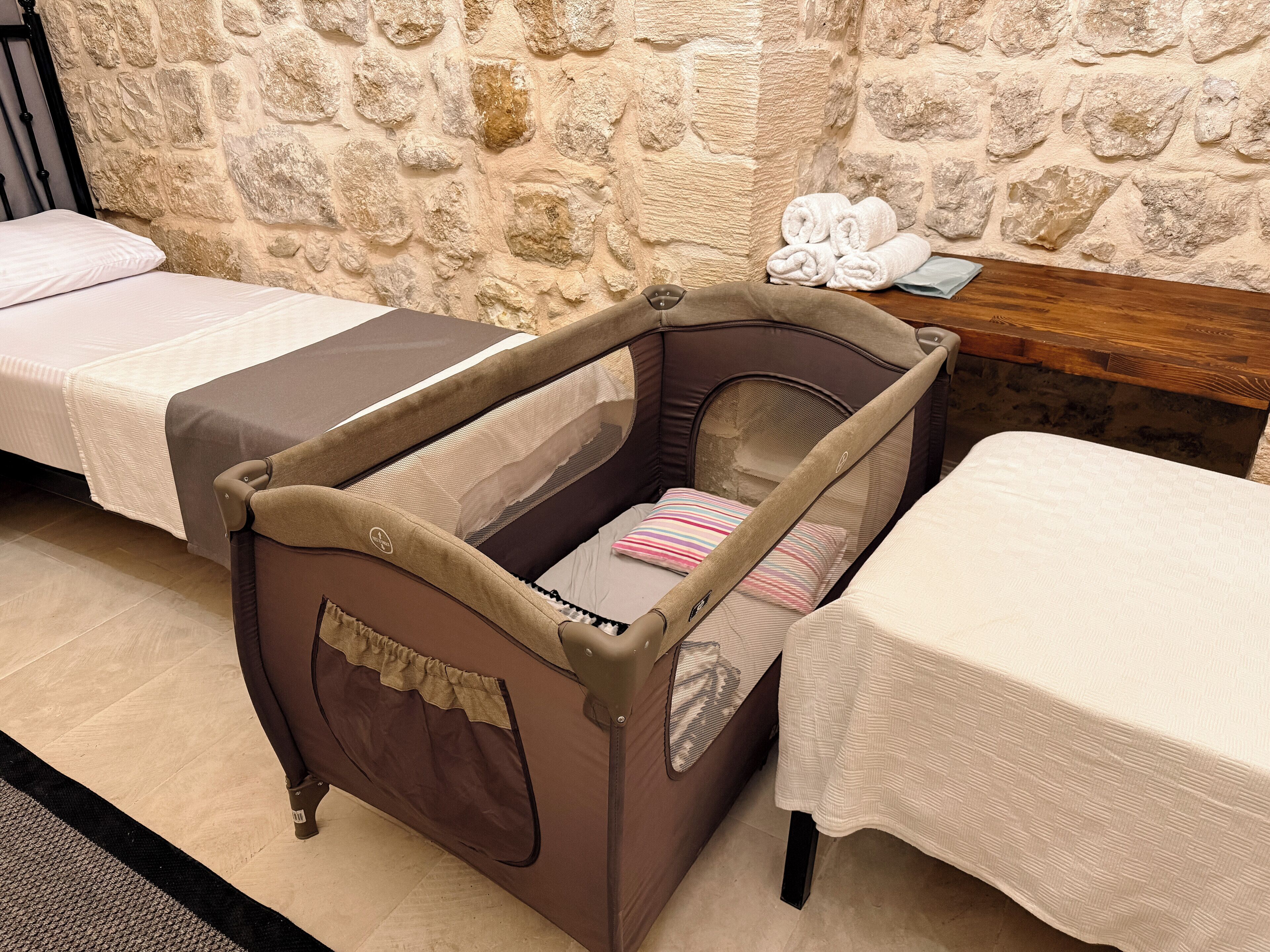 Quarto com berço de bebê, cama e banco de madeira.
