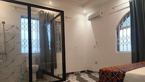 Quarto com cama, banheiro com vaso sanitário e chuveiro, e um espelho grande.
