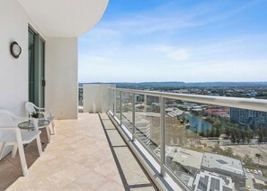 Uma varanda com vista ampla da cidade, guarda-corpo de vidro e área de estar com cadeiras e mesa.
