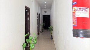 Um corredor com extintor preso à parede, portas e plantas em vasos.