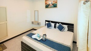 Quarto de hotel com cama, ventilador de teto, um quadro e um porta-toalhas.