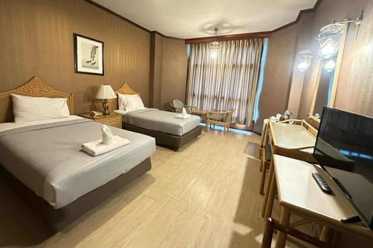 Quarto de hotel com duas camas, uma escrivaninha com cadeira, televisão e janela com cortinas.