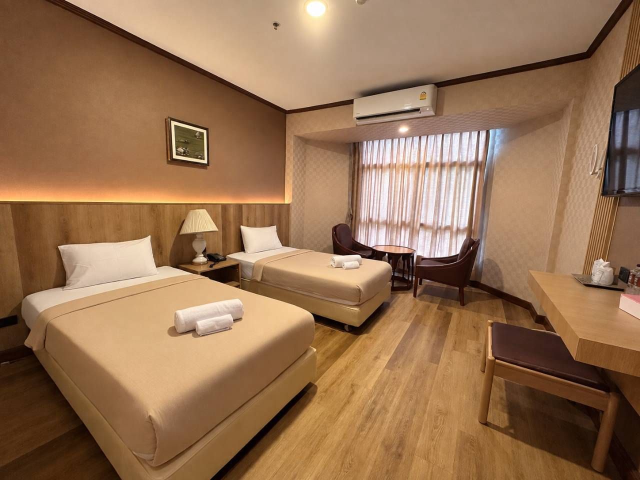 Quarto de hotel com duas camas, uma escrivaninha, uma cadeira, uma mesa, unidade de ar condicionado e janela com cortinas.